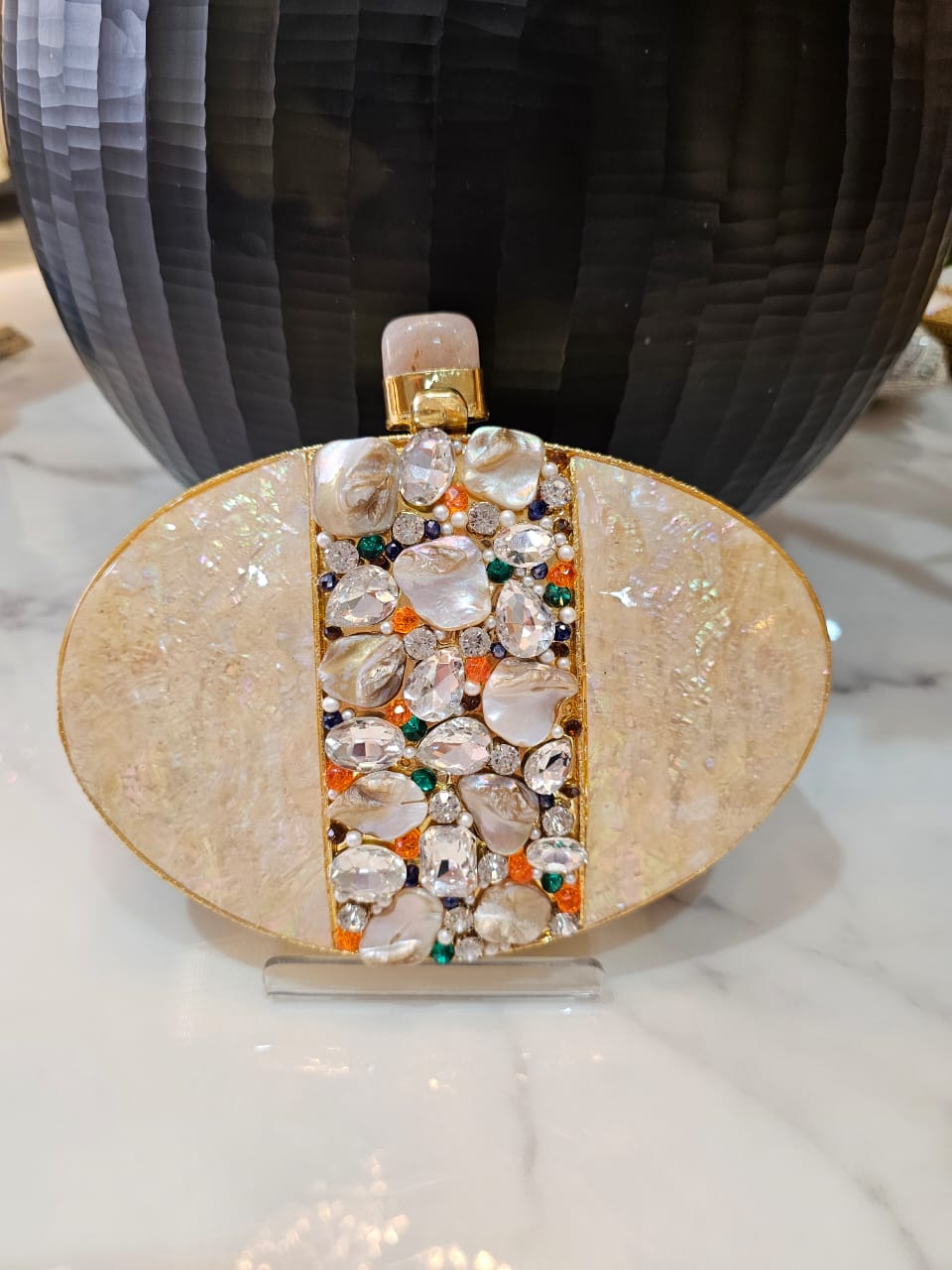 Oval metallic clutch with shell crystal colouring moti in middle and ...